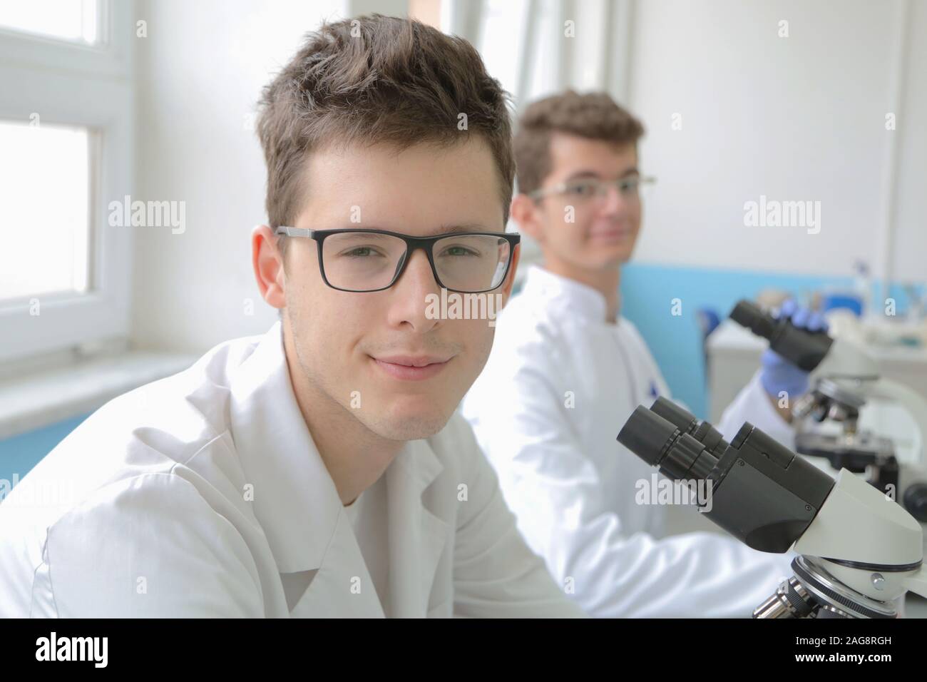 Two Young male scientists looking through a microscope in a laboratory ...