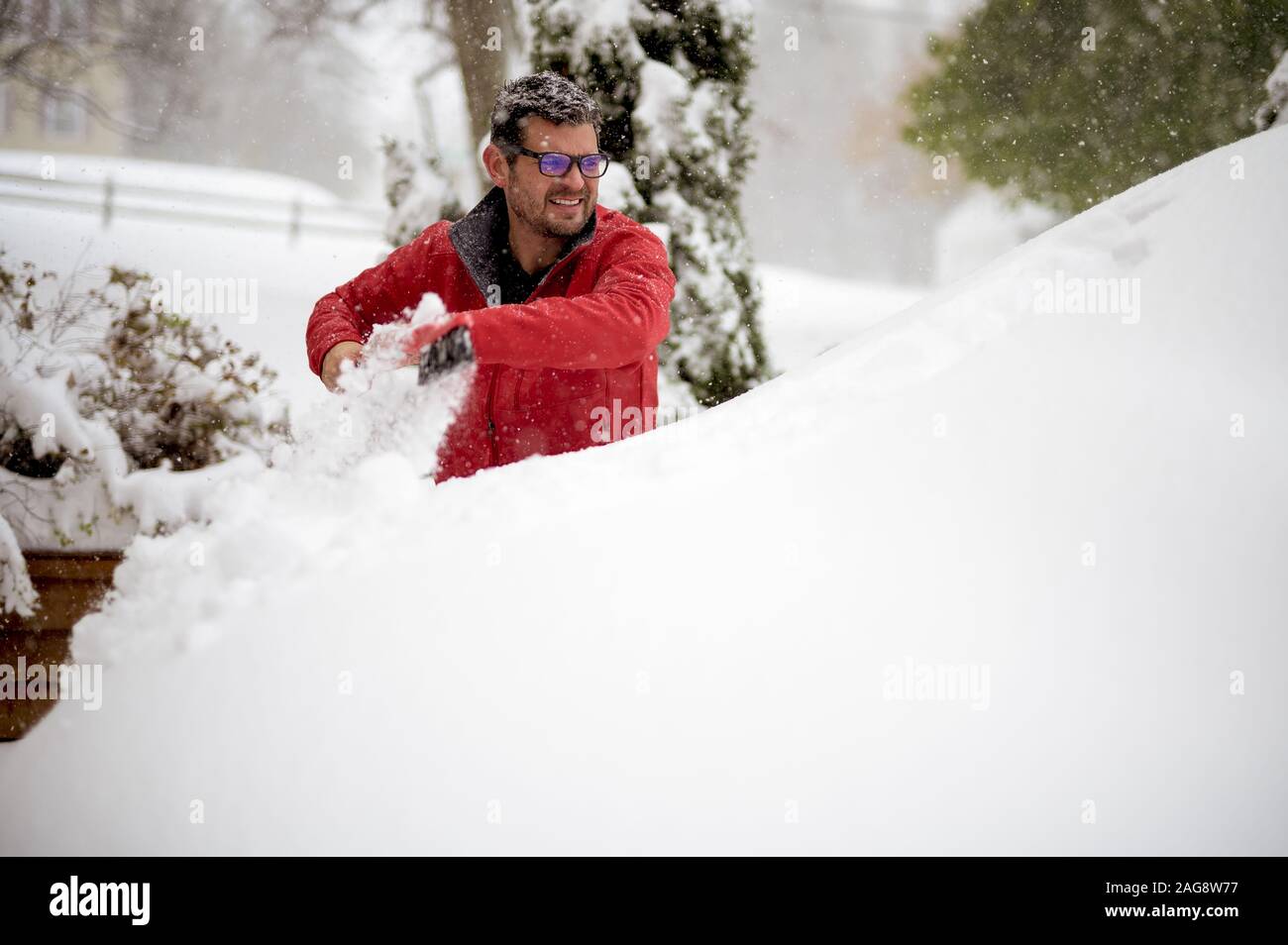 Male wearing a red winter jacket cleaning snow with his hands and a ...
