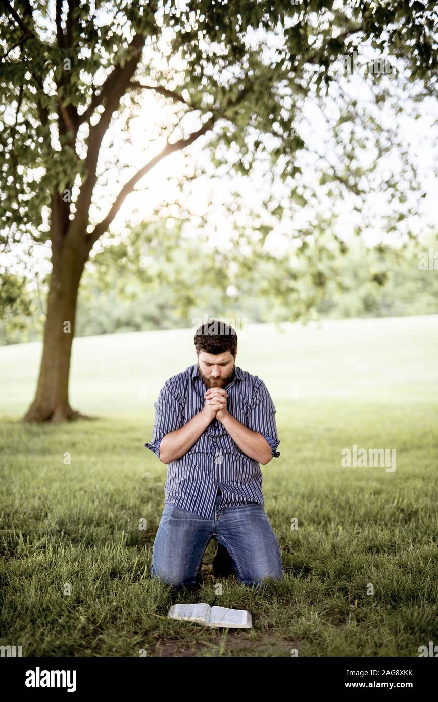 Vertical shot of a male on his knees with the bible in front of him ...
