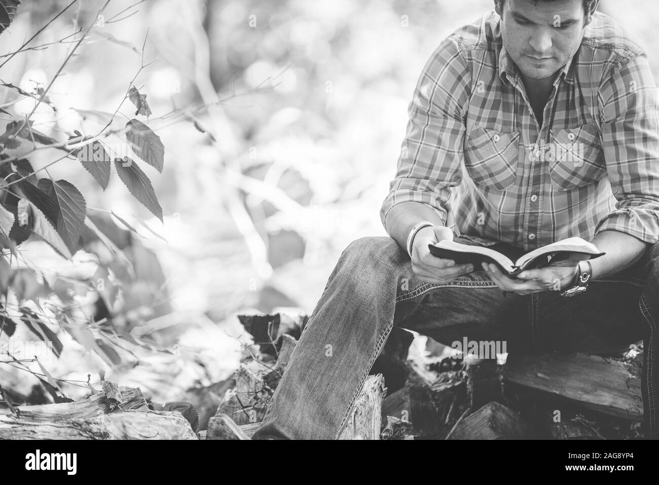 Grayscale closeup shot of a male sitting and reading the bible with a ...