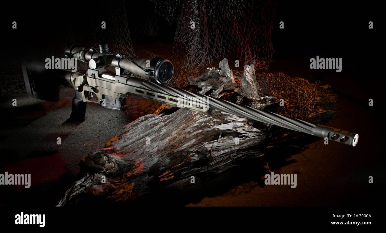 Sniper rifle and rifle scope behind a log with netting to hide the ...