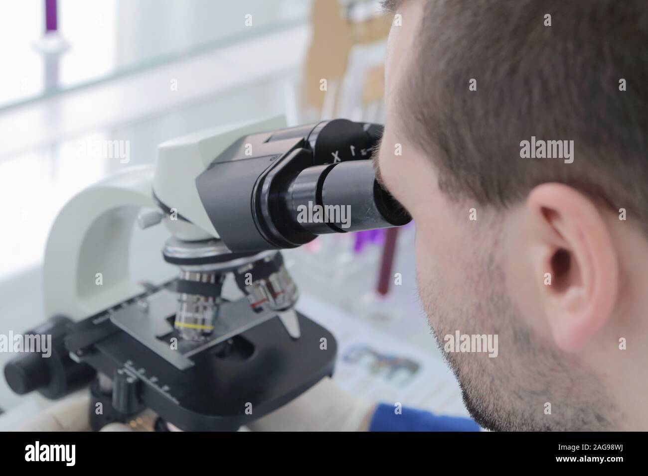 Young male male scientist looking through a microscope in a laboratory ...