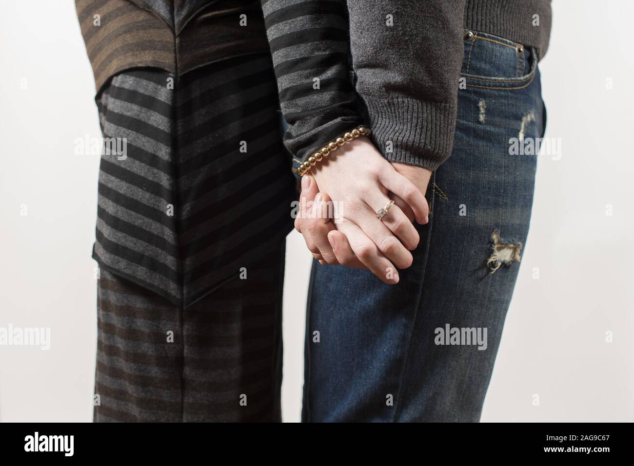 Closeup shot of a couple standing back to back while holding hands with ...