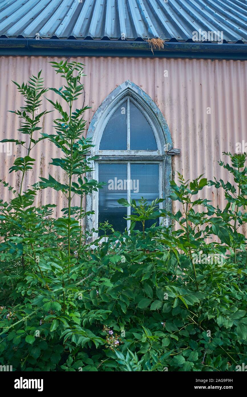 A arched window made from wood that is decaying in a building that has ...