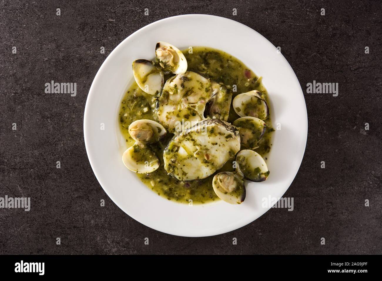 Hake fish and clams with green sauce on black background. Typical ...