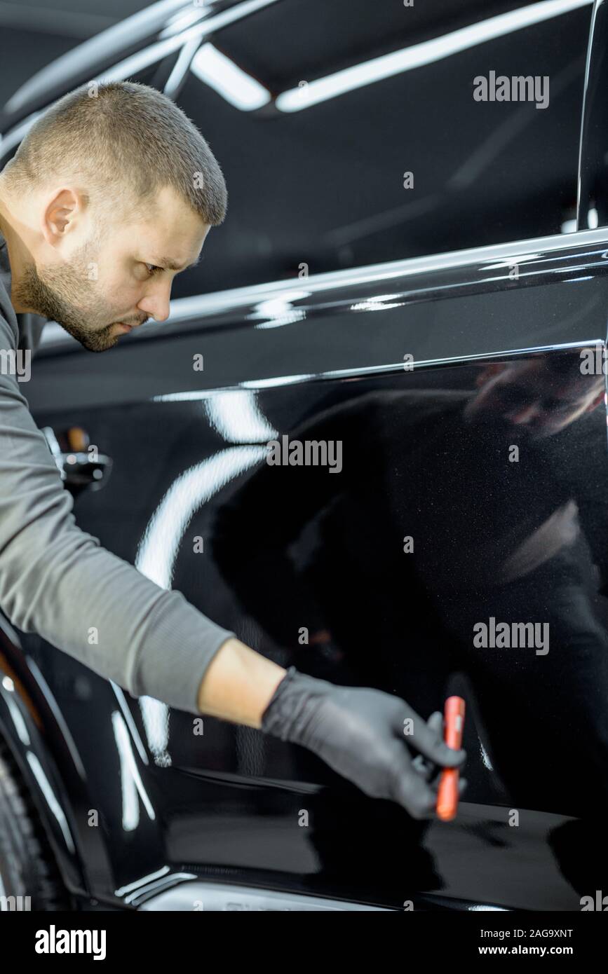 Worker examining vehicle body for scratches and damages backliting by a ...
