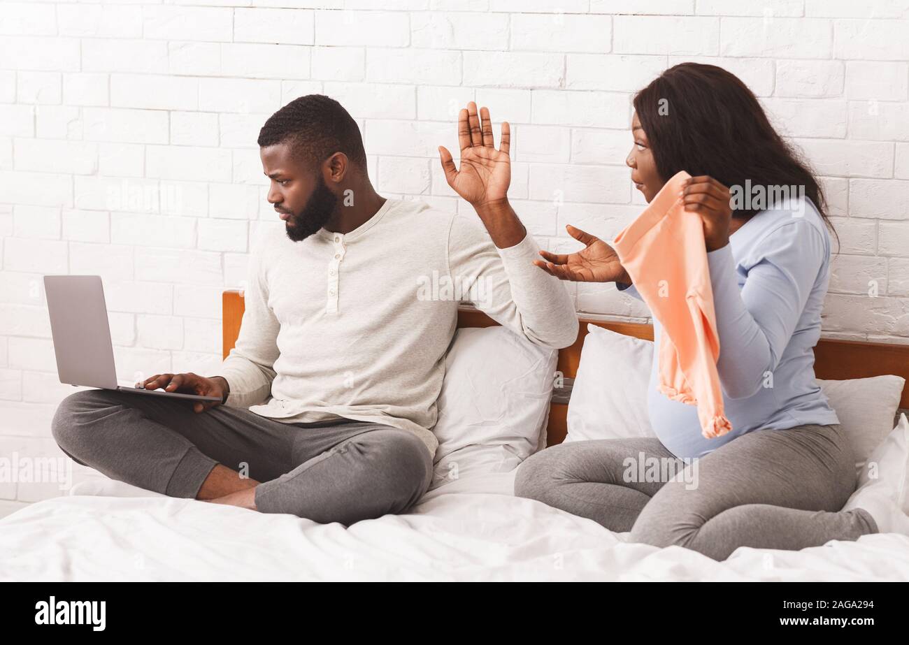 Expecting lady showing her busy husband baby clothes Stock Photo - Alamy