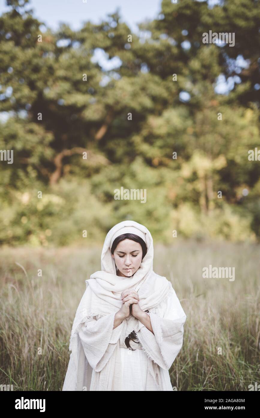 Vertical shot of a female wearing a biblical robe and praying while her ...