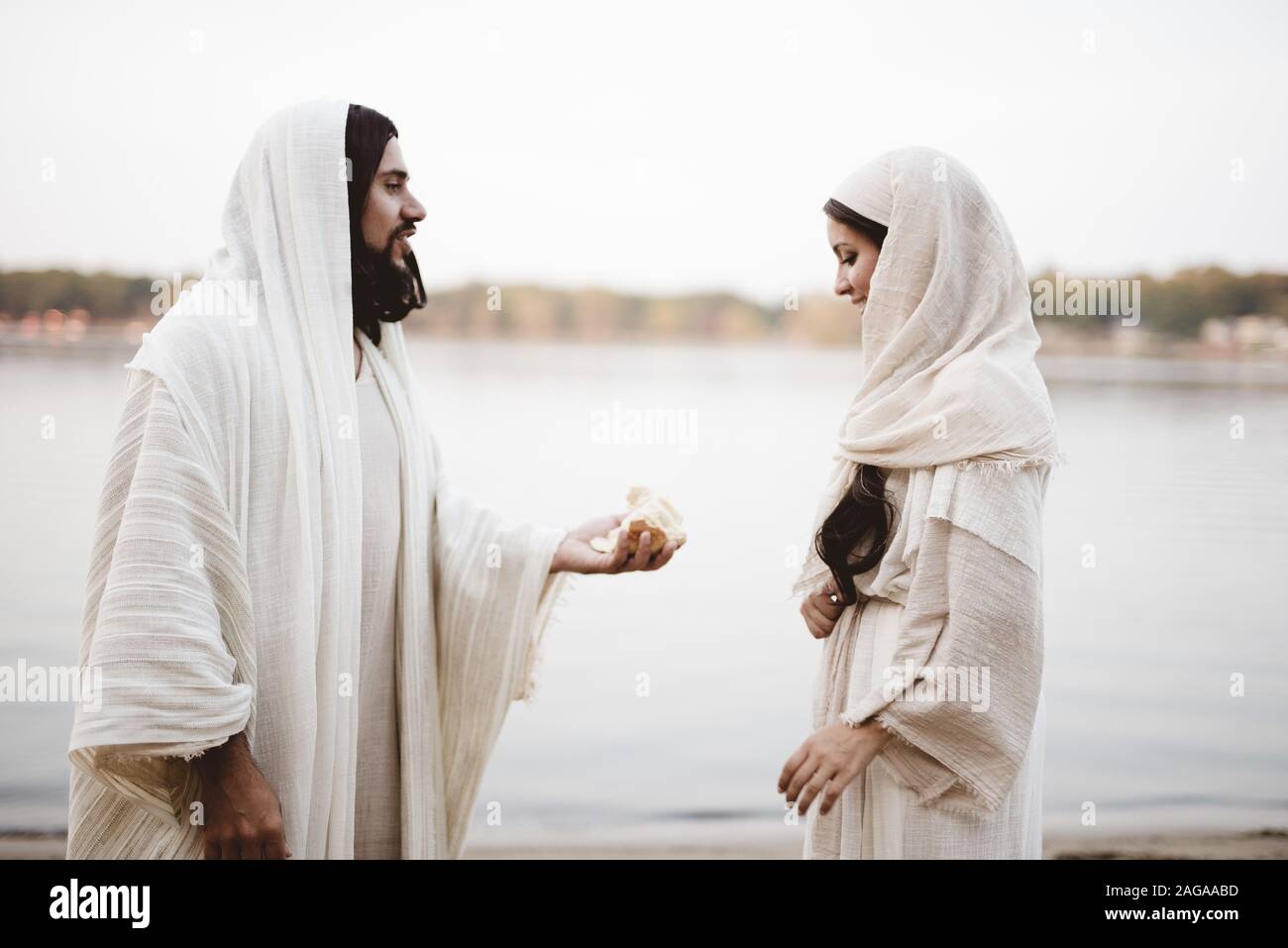 Shallow focus shot of Jesus Christ offering peace of bread to a female ...