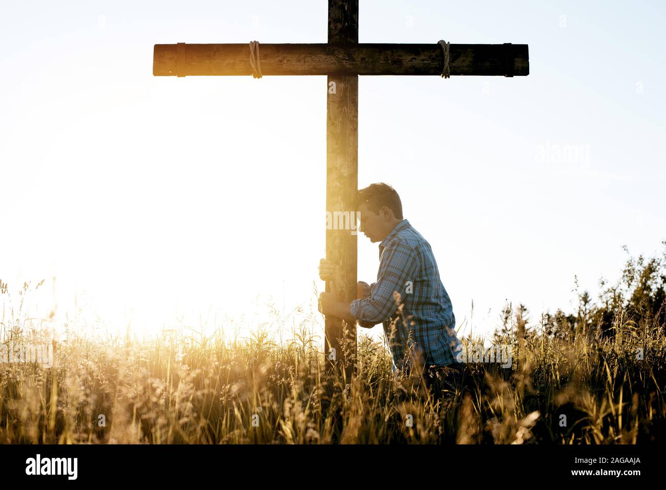 Male with his head leaned against a hand made wooden cross while ...