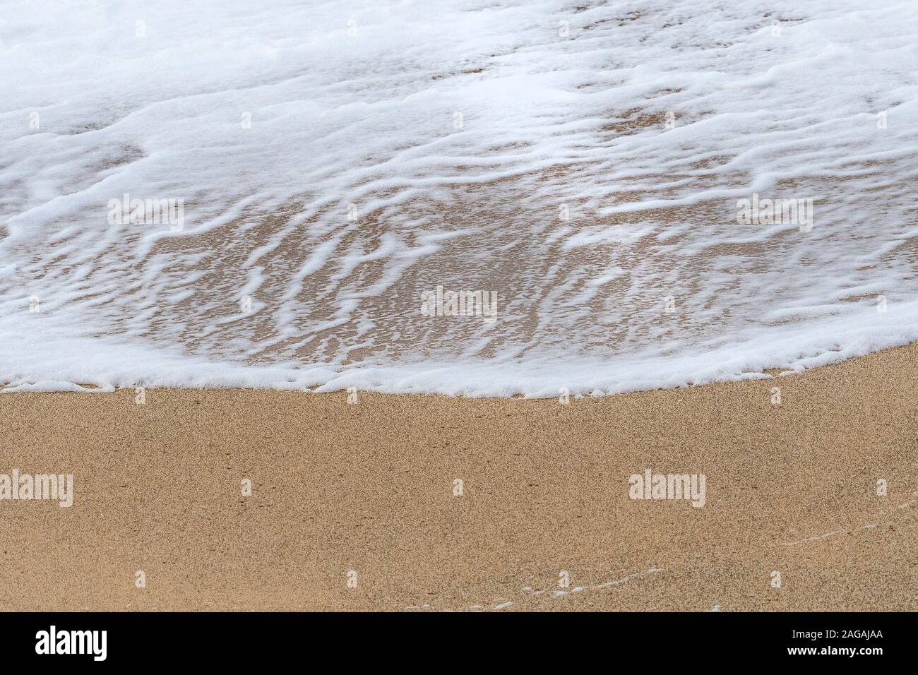 The foam of a small wave left behind on a beach as the wave recedes ...