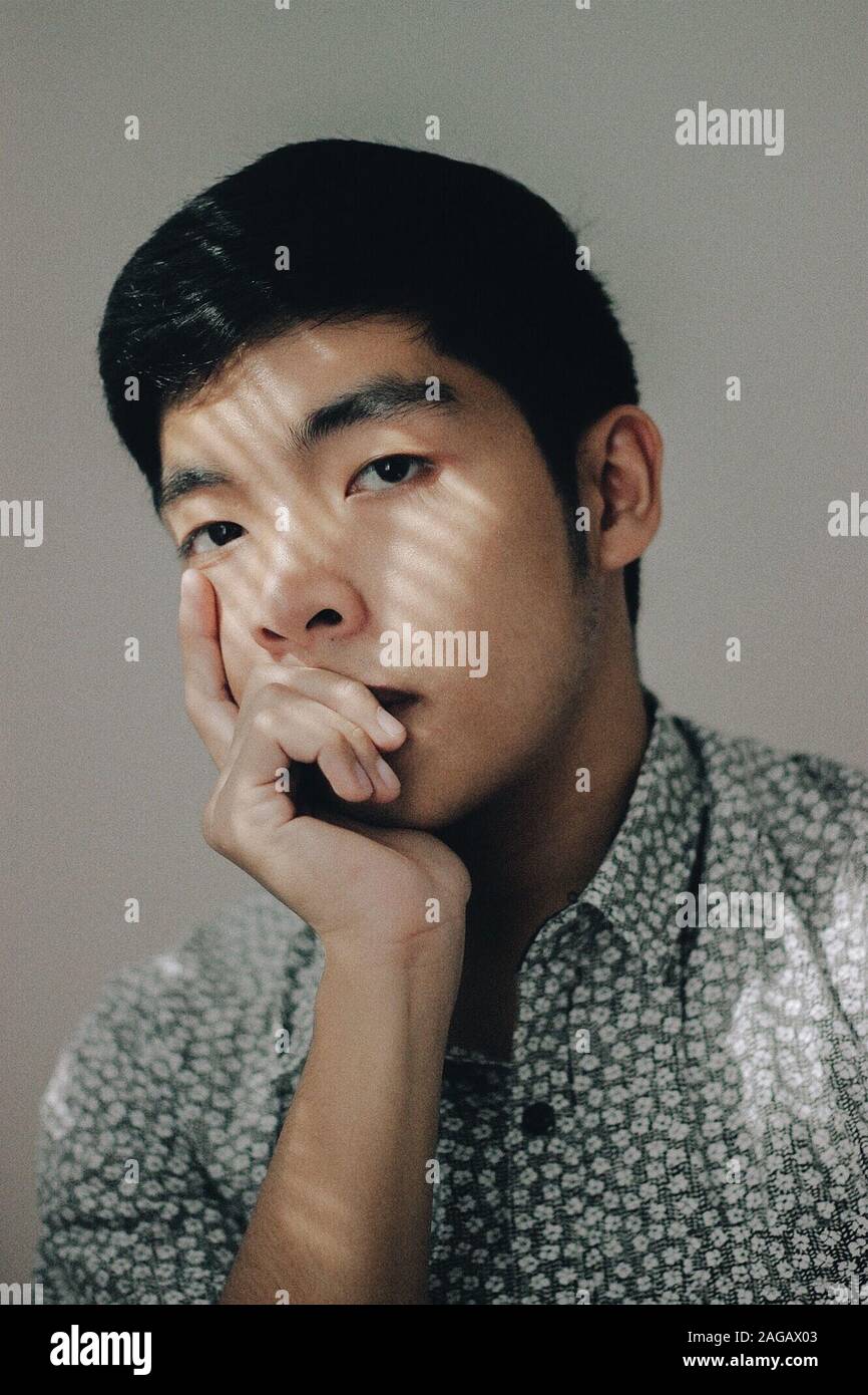 Vertical shot of Asian male thinking with his hand under the chin on ...