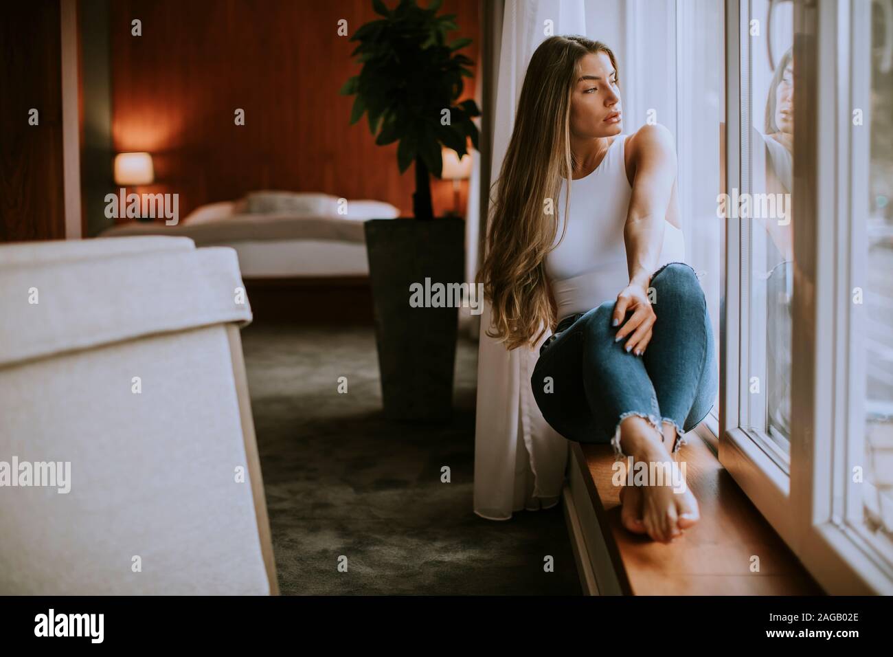 Beautiful young woman sitting by the window in apartment Stock Photo ...