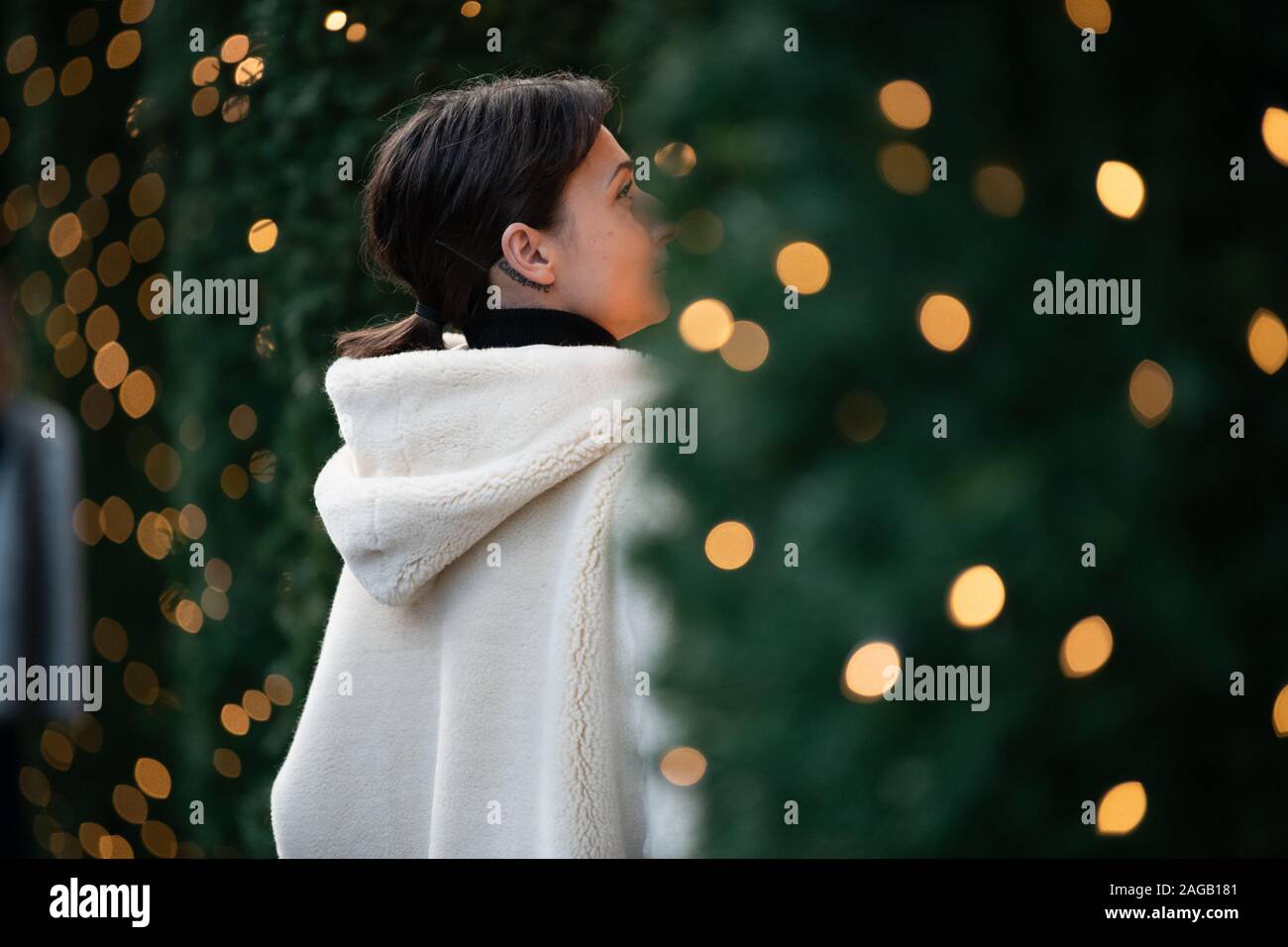 Young woman looking up at a shop window, light reflecting in her face ...