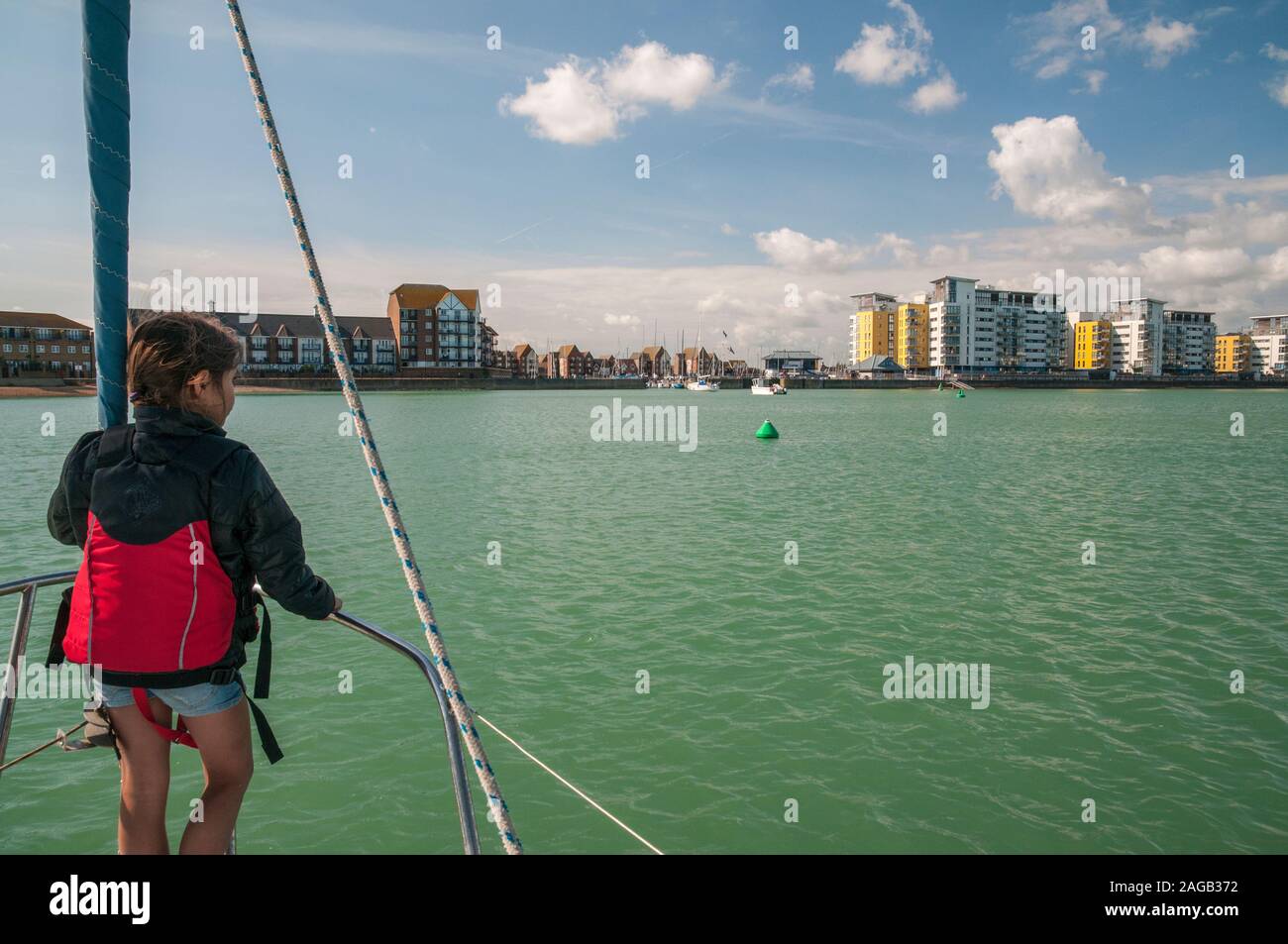 Young girl with red life jacket standing at the bow of a yacht ...