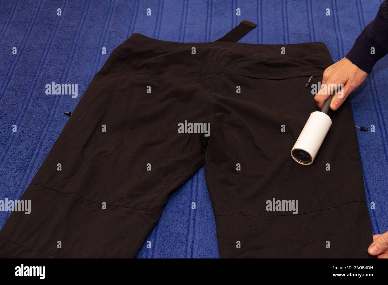 female hand with sticky roller for cleaning clothes cleans black mens ...