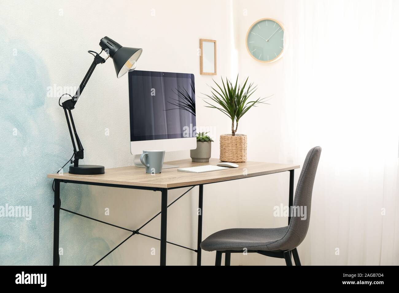 Workplace with computer, lamp and plant on wooden table. Light blue and ...