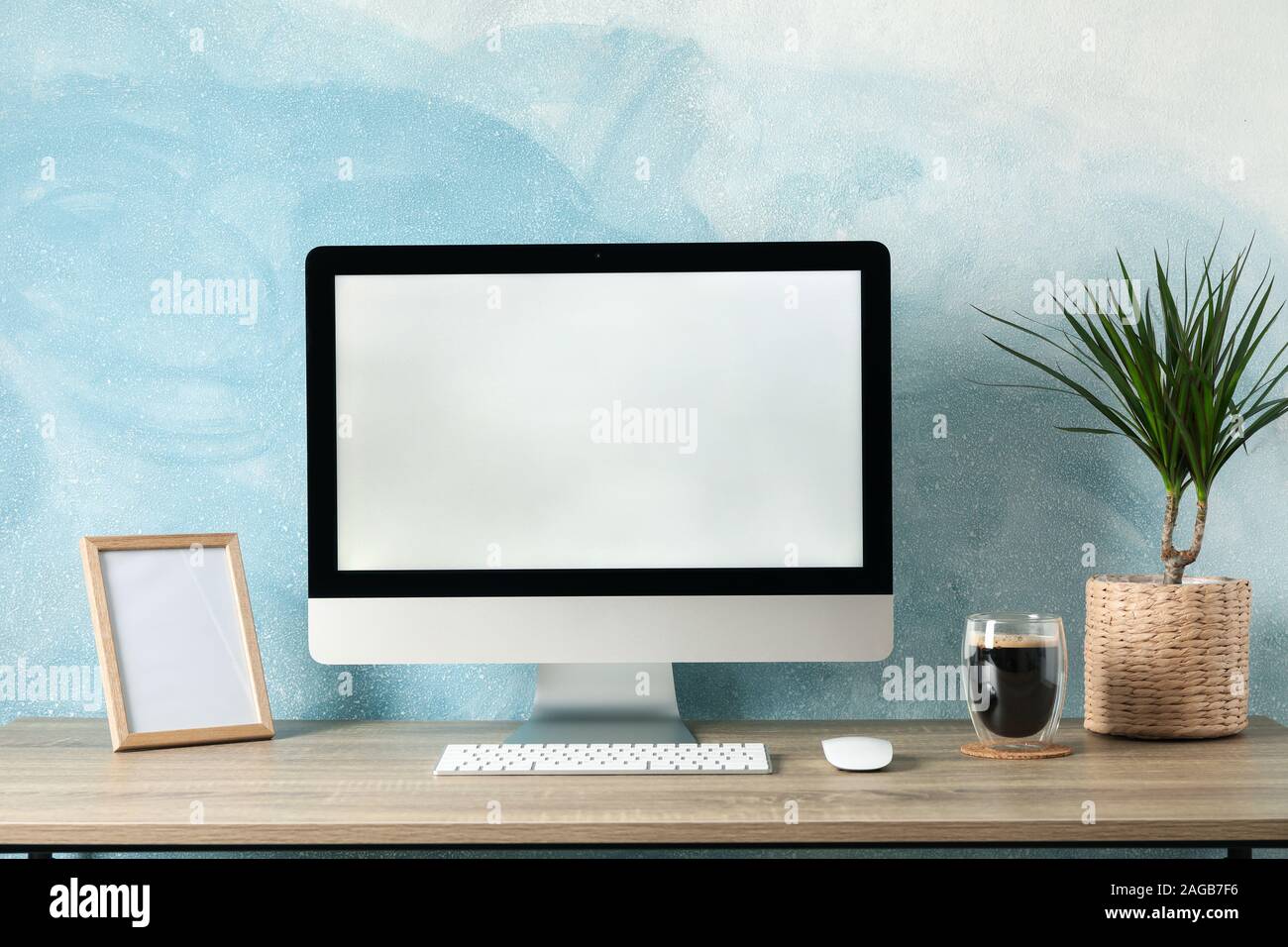 Workplace with computer and plant on wooden table. Blue background ...