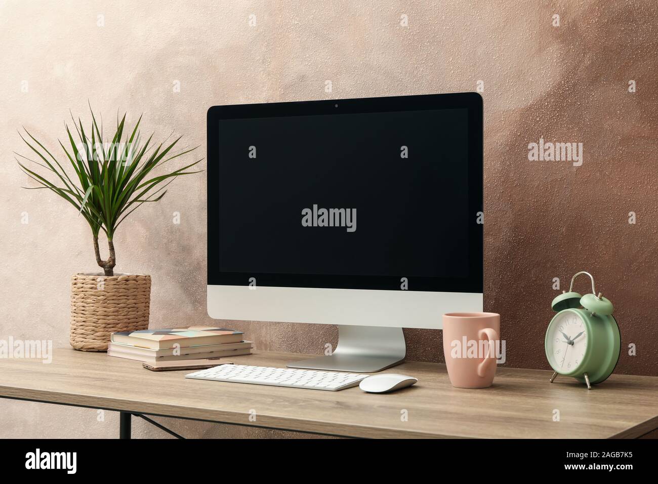 Workplace with computer and plant on wooden table. Light brown ...