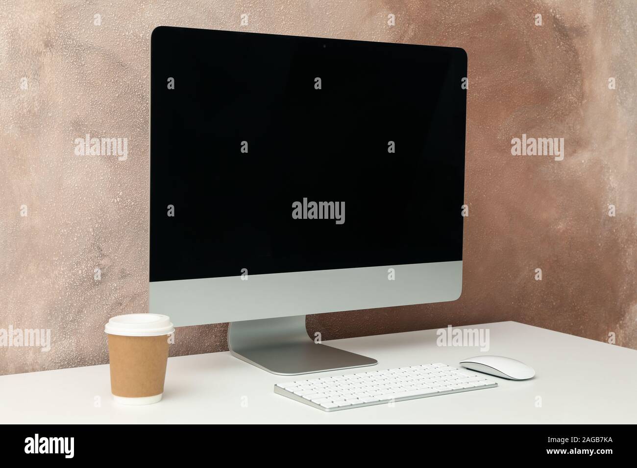 Workplace with computer and cup on white table. Light brown background ...
