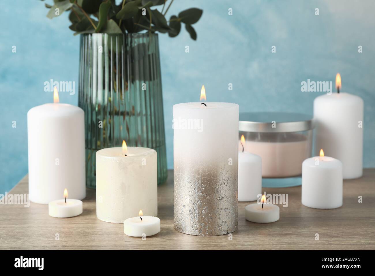 Burning candles and vase with eucalyptus against blue background, close ...