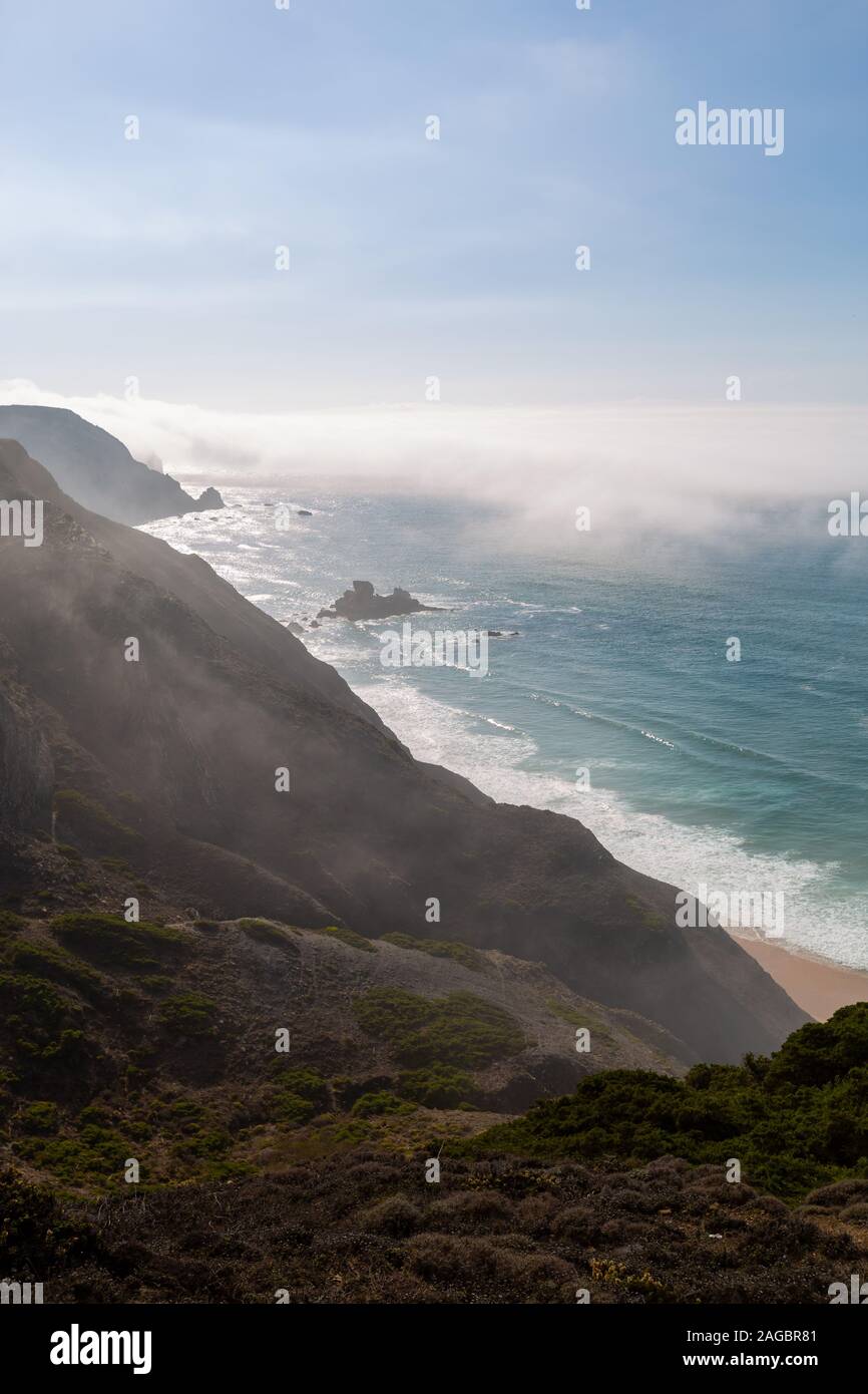 Vertical picture of a sea covered in a fog surrounded by hills and ...