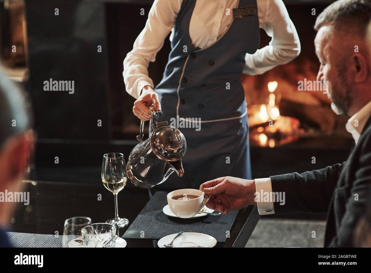 Warm atmosphere. Female waiter pouring hot tea in the white cup ...