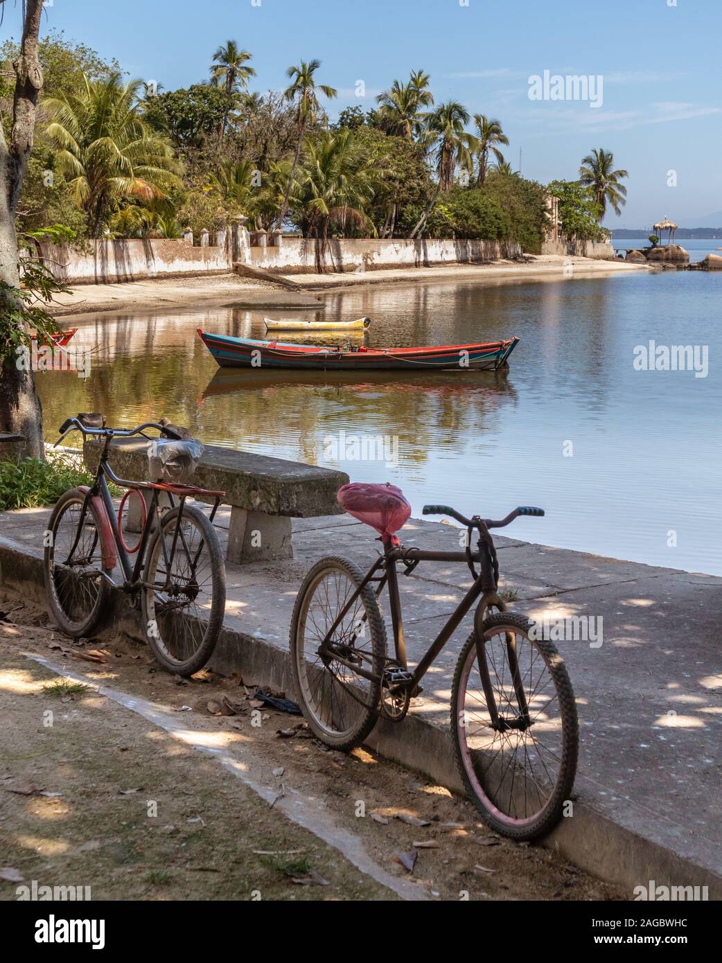 Two bicycles standing in the shade, with boat, sea and trees in the ...