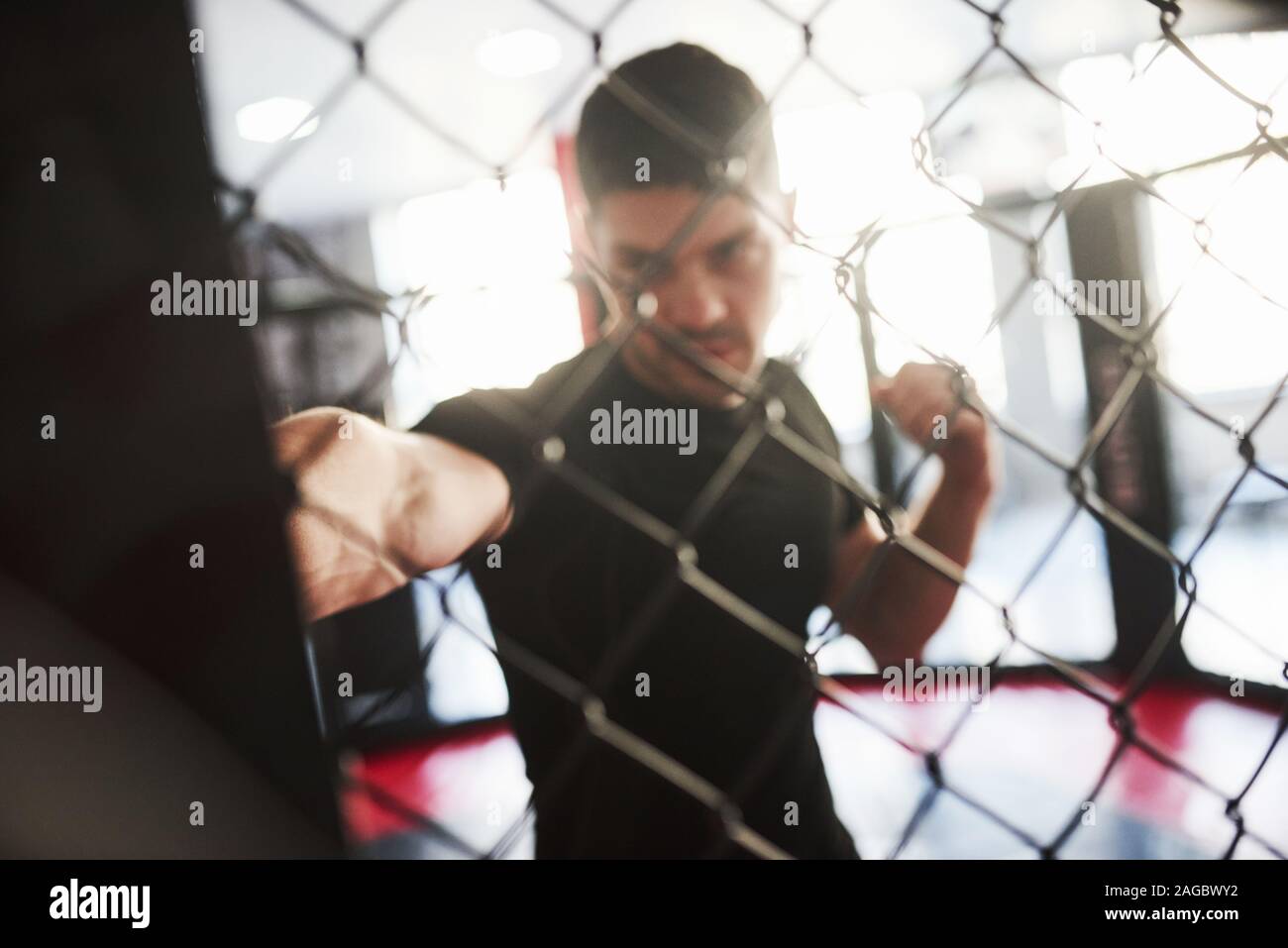 Blurred picture. Strong man is boxing in the gym behind the fence ...