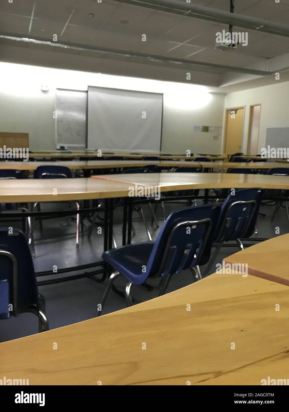Vertical shot of an empty classroom with blue chairs and wooden tables ...