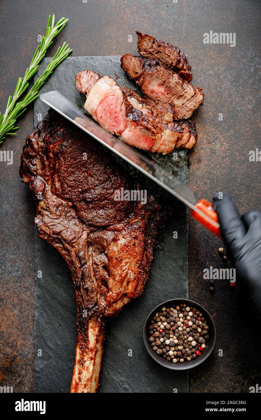 Hand in black gloves cuts dry-aged marble beef steak Tomahawk. Top view ...