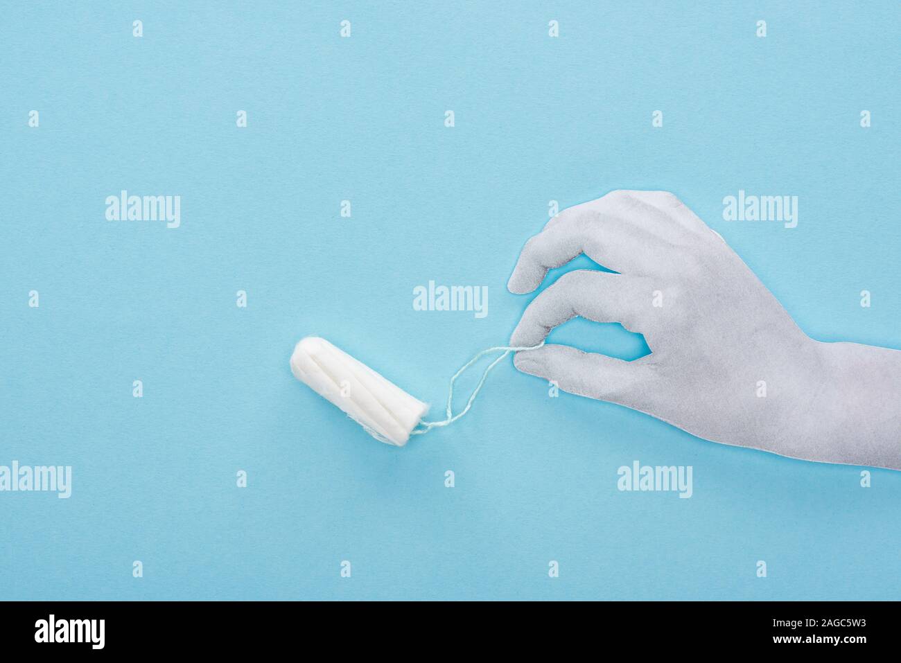 top view of white paper cut hand holding cotton tampon on blue ...