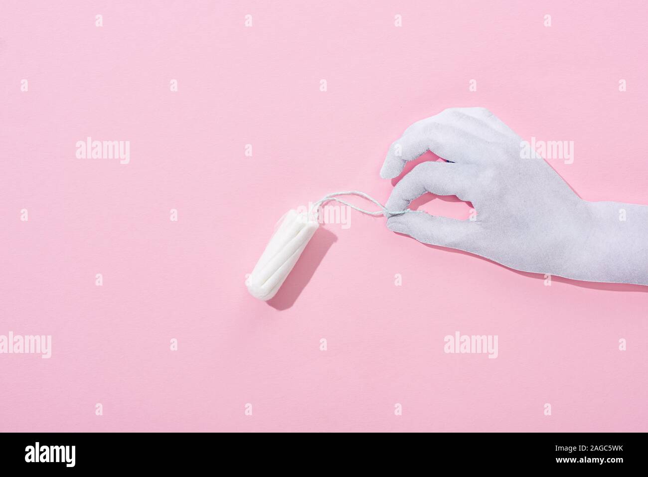top view of white paper cut hand holding cotton tampon on pink ...