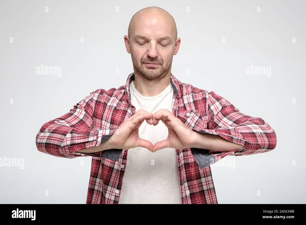 Portrait of a bald, unshaven man who is trying to make a heart shape ...