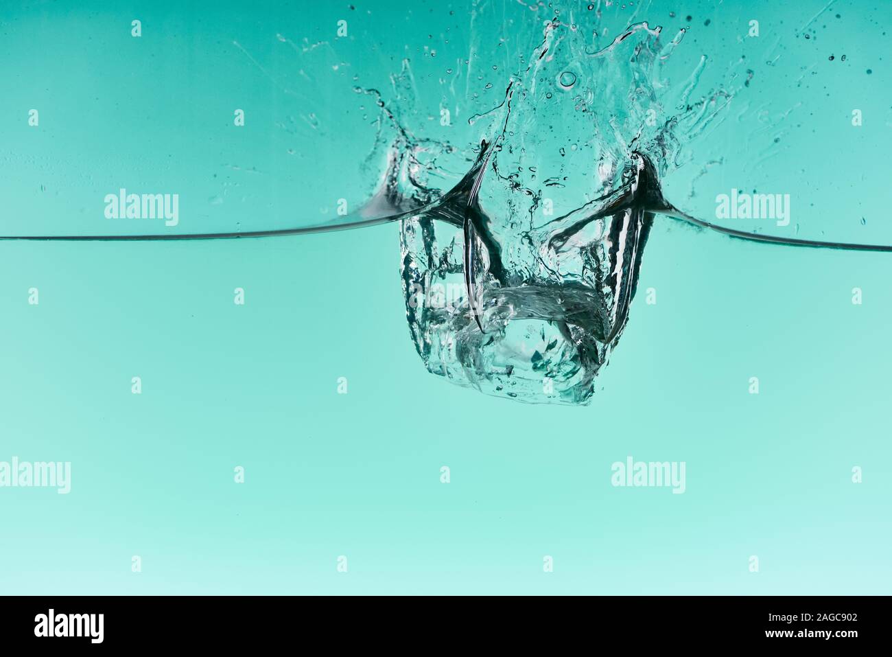 transparent ice cubes falling in water with splash on turquoise ...