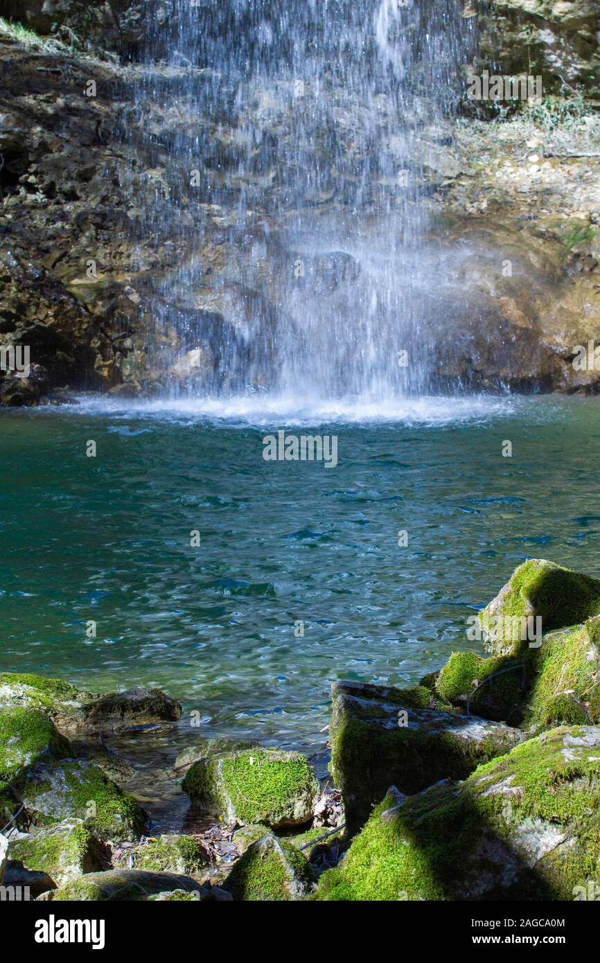 Vertical shot of stones covered with moss in a lake under the Waterfall ...
