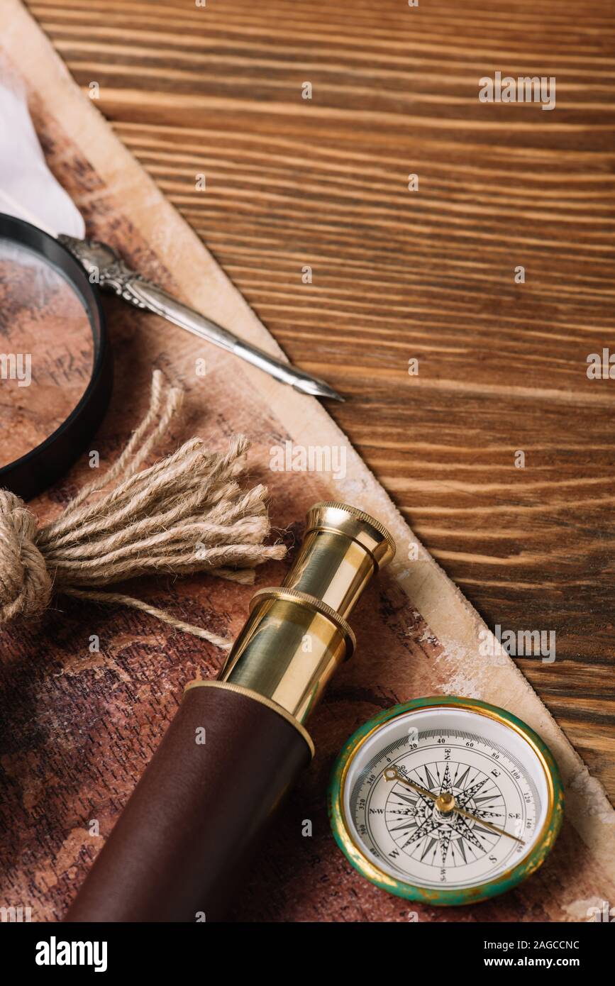 top view of map, nib, compass, rope and telescope on wooden surface ...