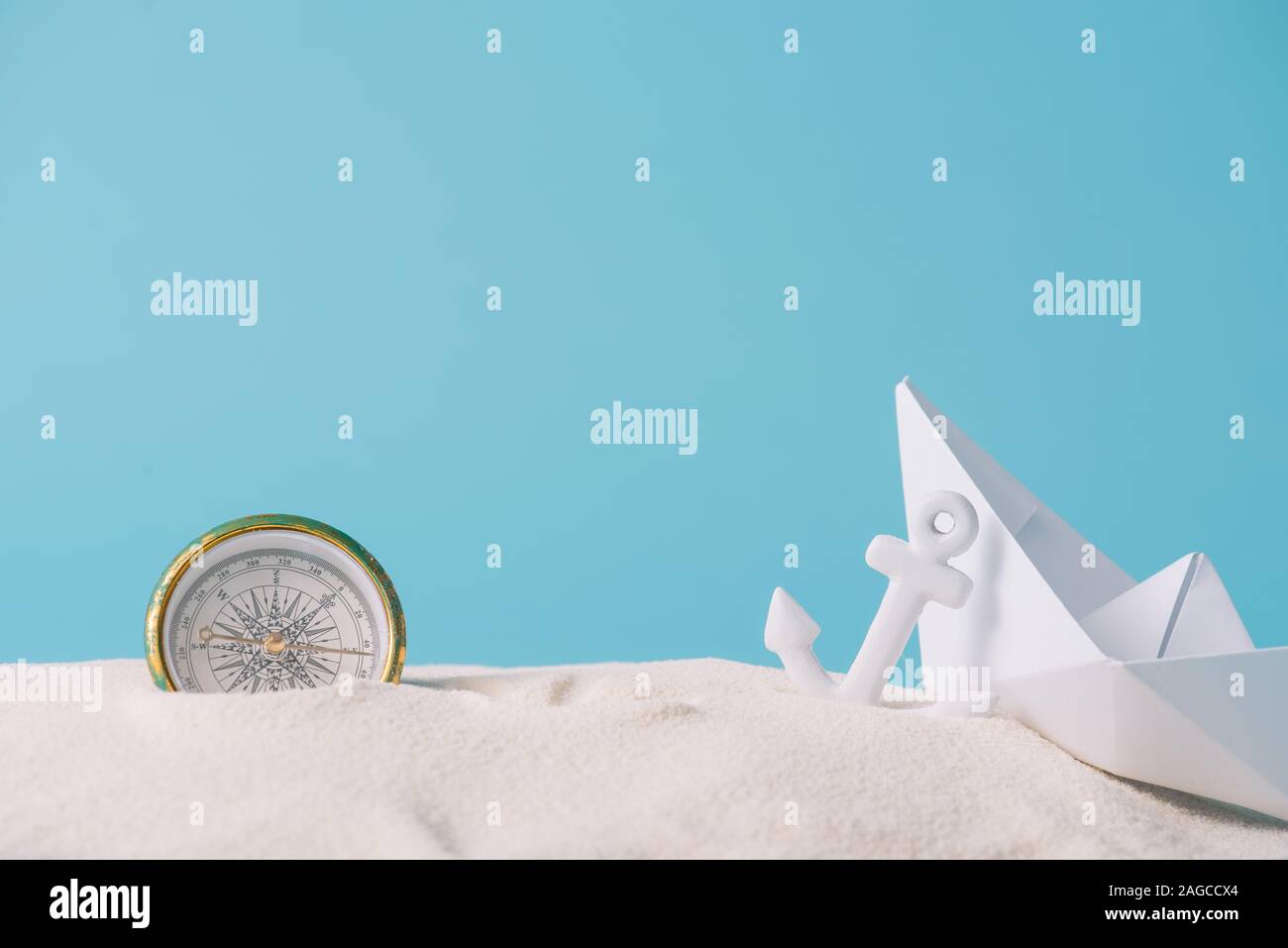 white sand with paper boat, compass and anchor isolated on blue Stock ...