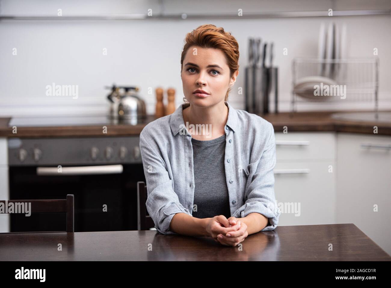 attractive woman sitting near table with clenched hands Stock Photo - Alamy