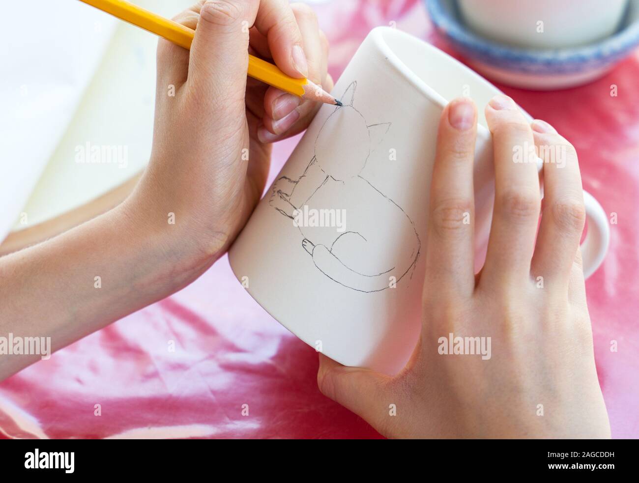 Child paints a mug in a pottery workshop. Drawing a cat Stock Photo - Alamy