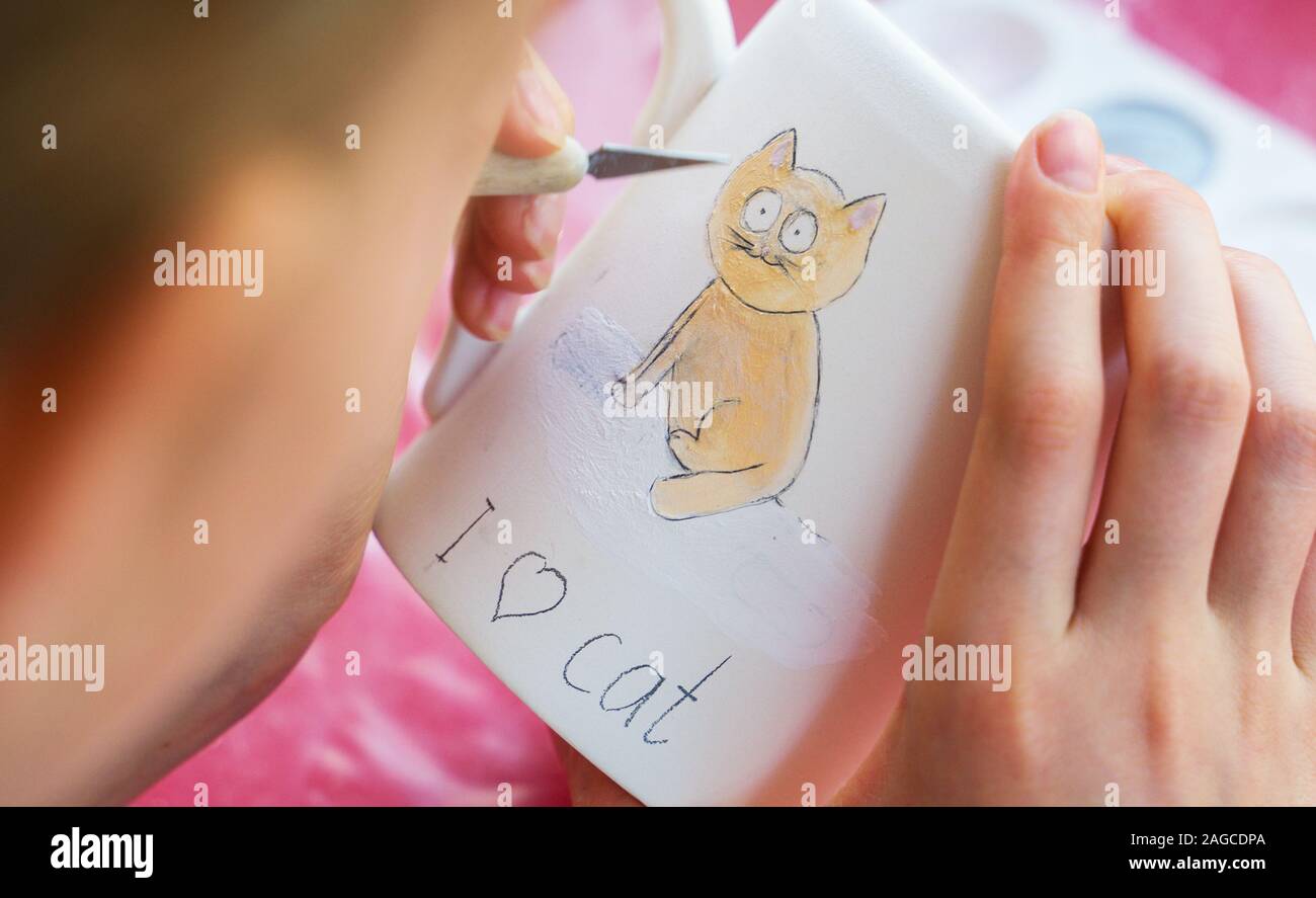 Child paints a mug in a pottery workshop. Drawing a cat Stock Photo - Alamy