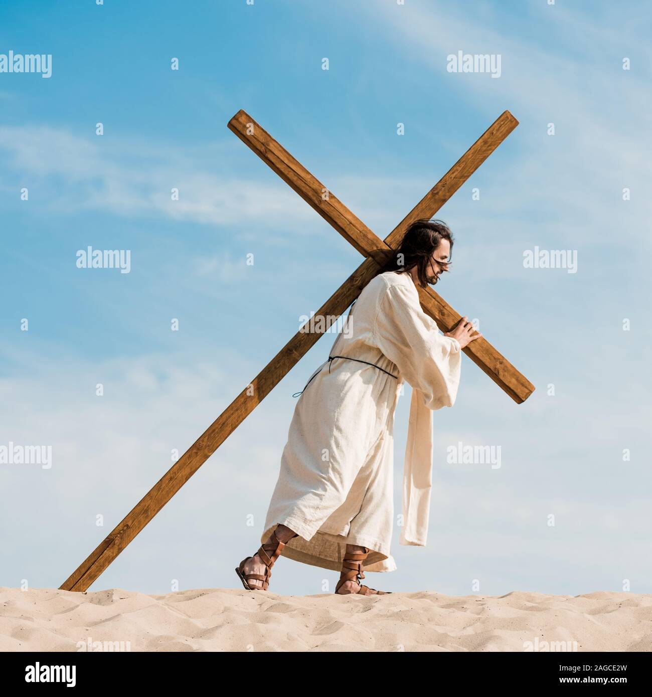 bearded man walking with wooden cross against blue sky in desert Stock ...