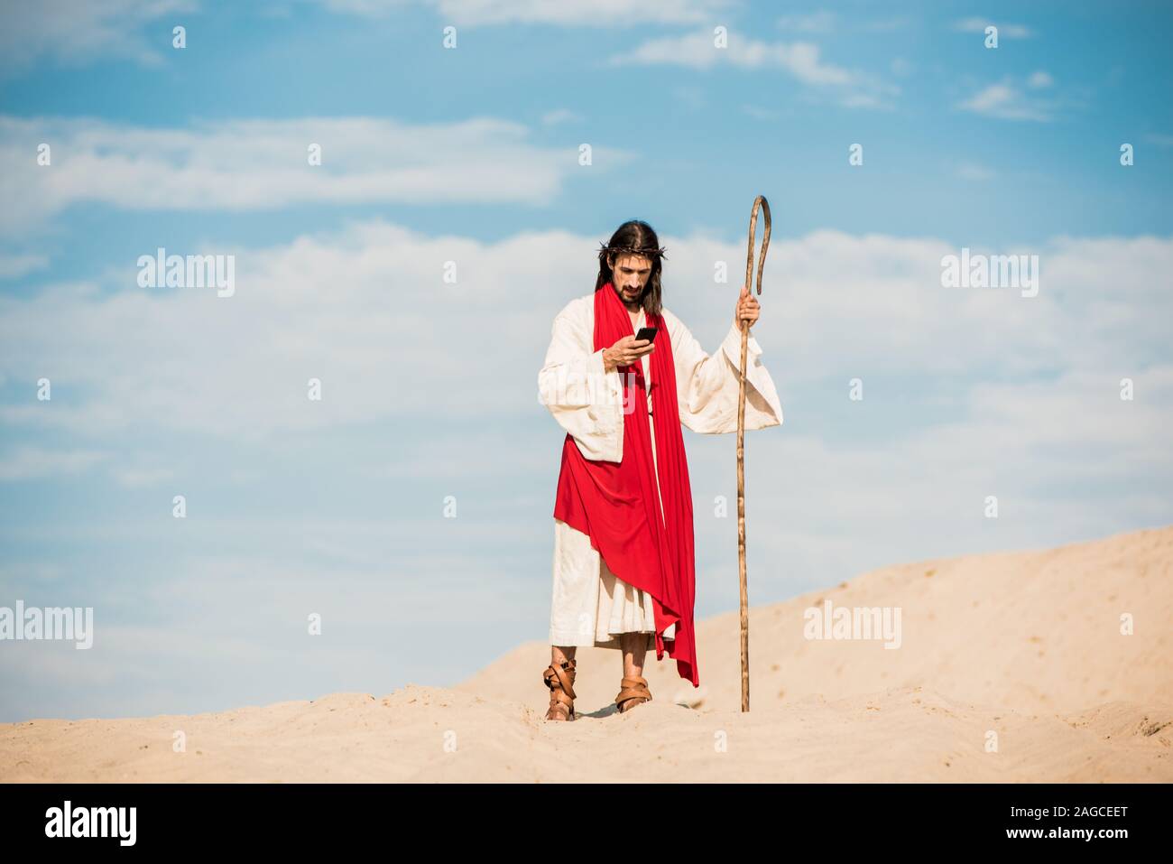 handsome man in jesus robe holding wooden cane and using smartphone in ...