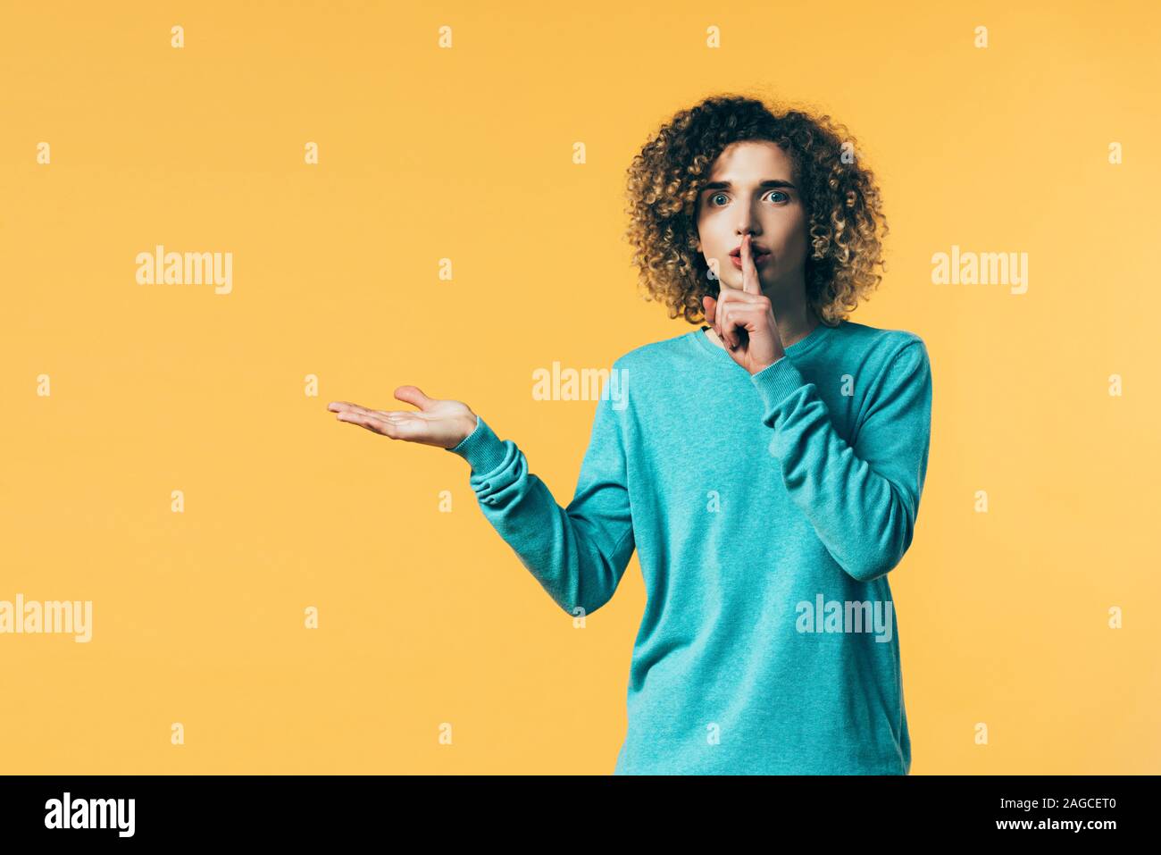 curly teenager showing shh gesture and pointing with hand aside ...
