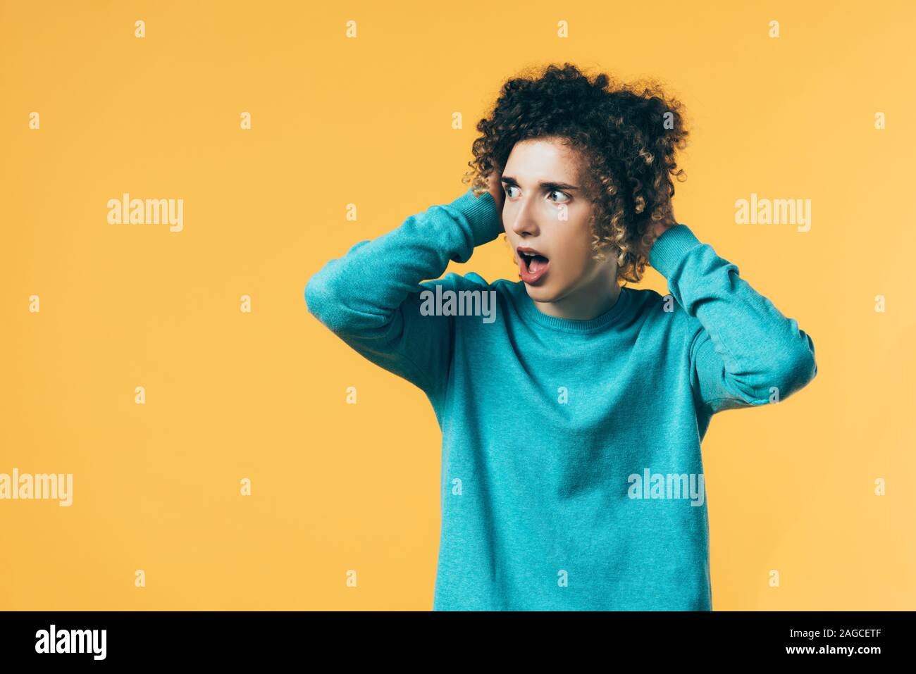 scared curly teenager with open mouth looking away isolated on yellow ...