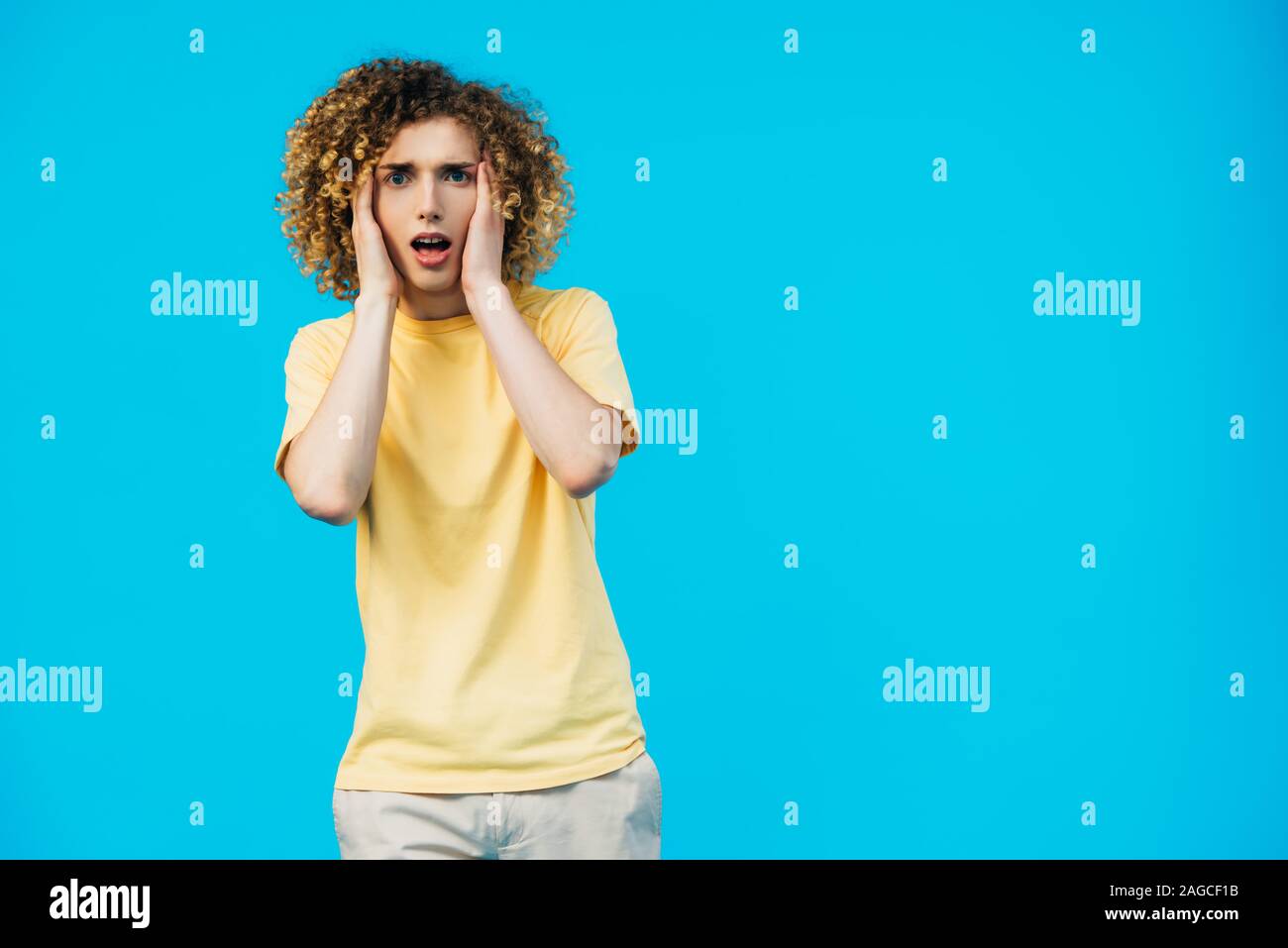 scared curly teenager with hands on head isolated on blue Stock Photo ...