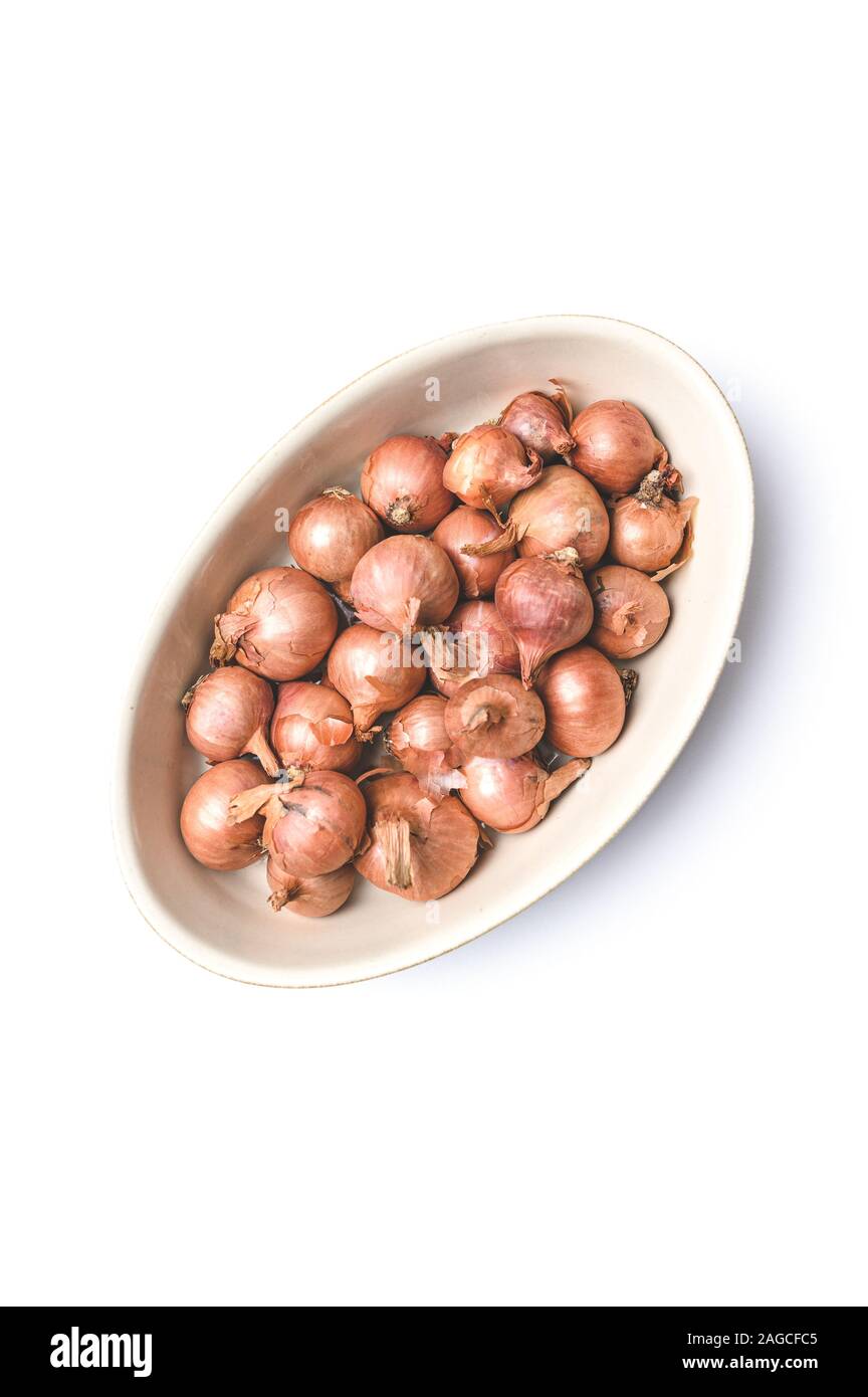 Vertical overhead shot of a bowl of raw shallots on a white surface ...