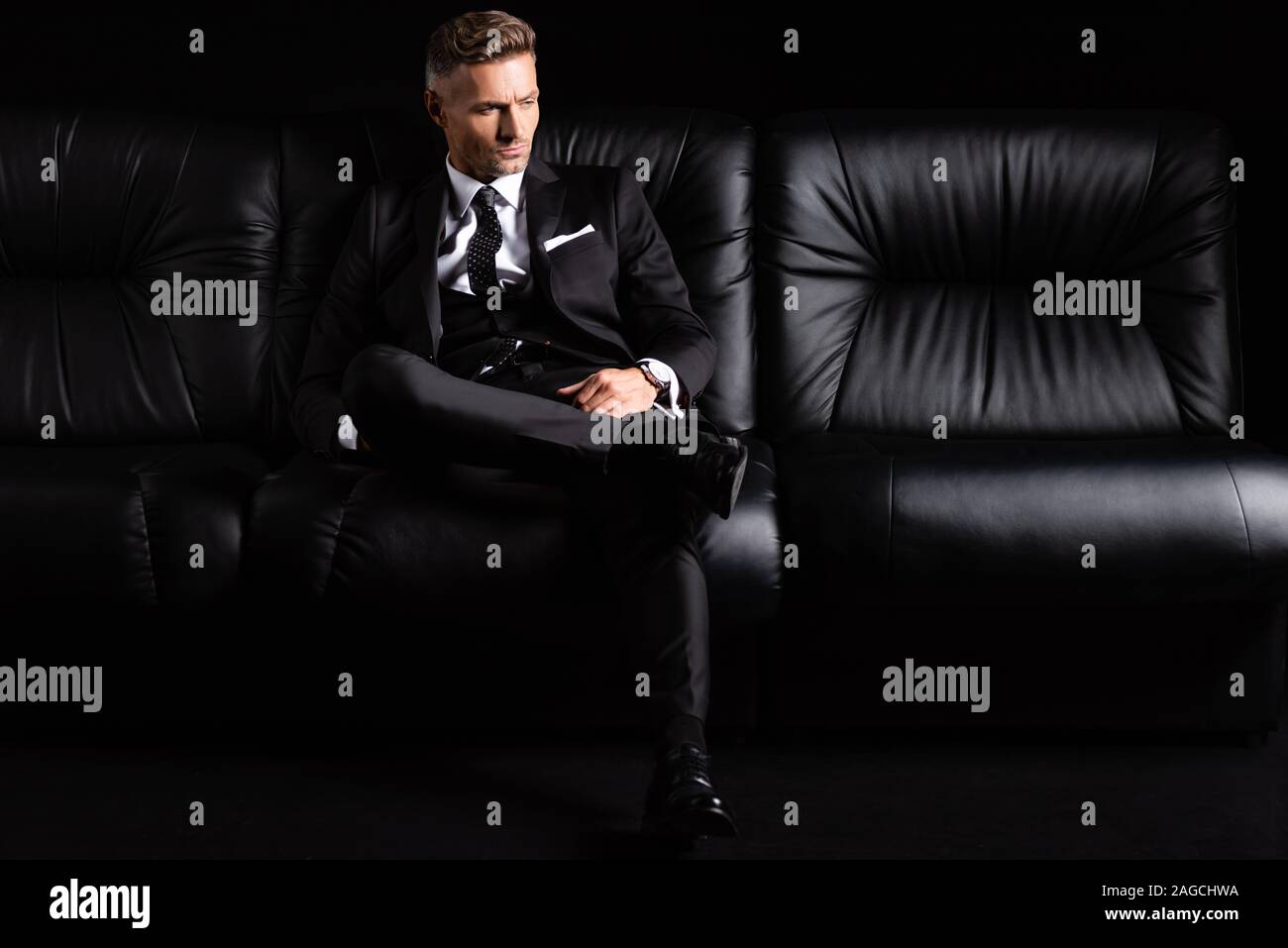 Confident businessman in formal wear sitting on couch isolated on black ...