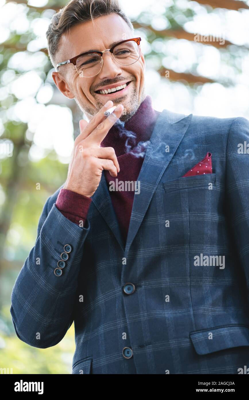 Handsome businessman smoking cigarette while smiling away outdoors ...