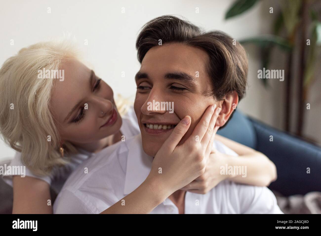 Smiling blonde girl touching boyfriend face at home Stock Photo - Alamy